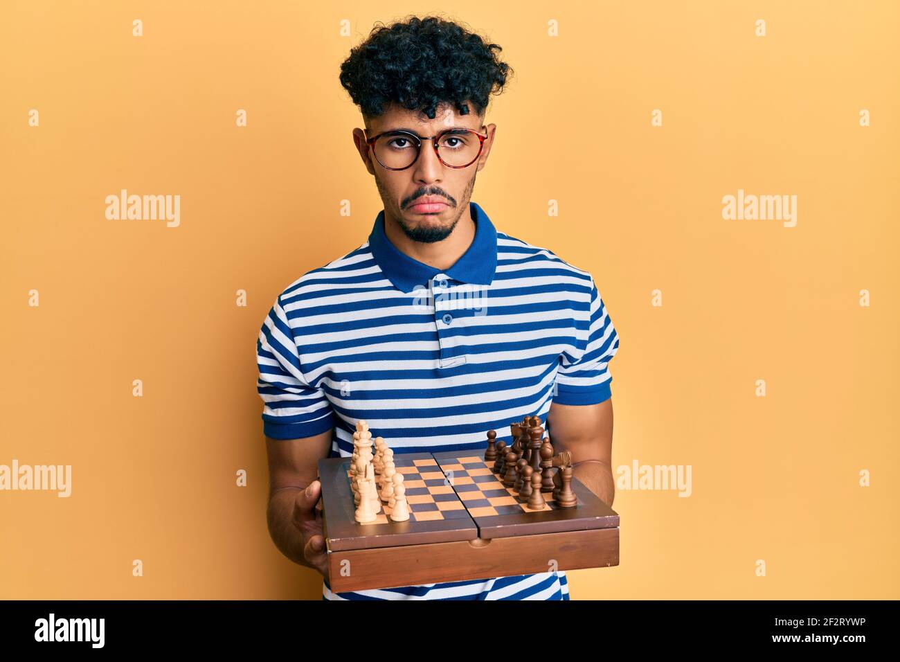 Young arab handsome man holding chess board wearing glasses depressed ...