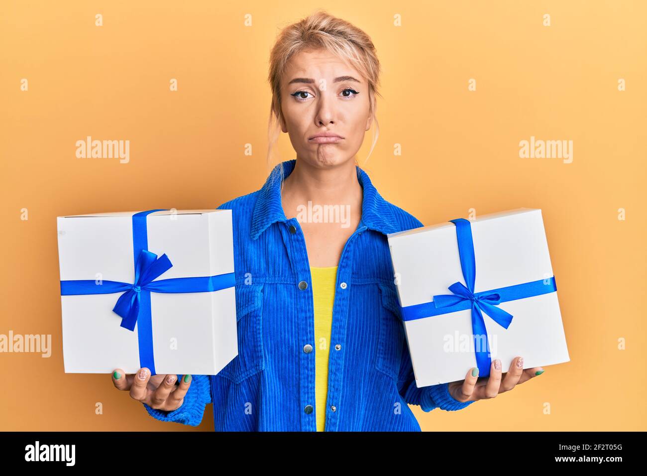 Young blonde girl holding gifts depressed and worry for distress ...