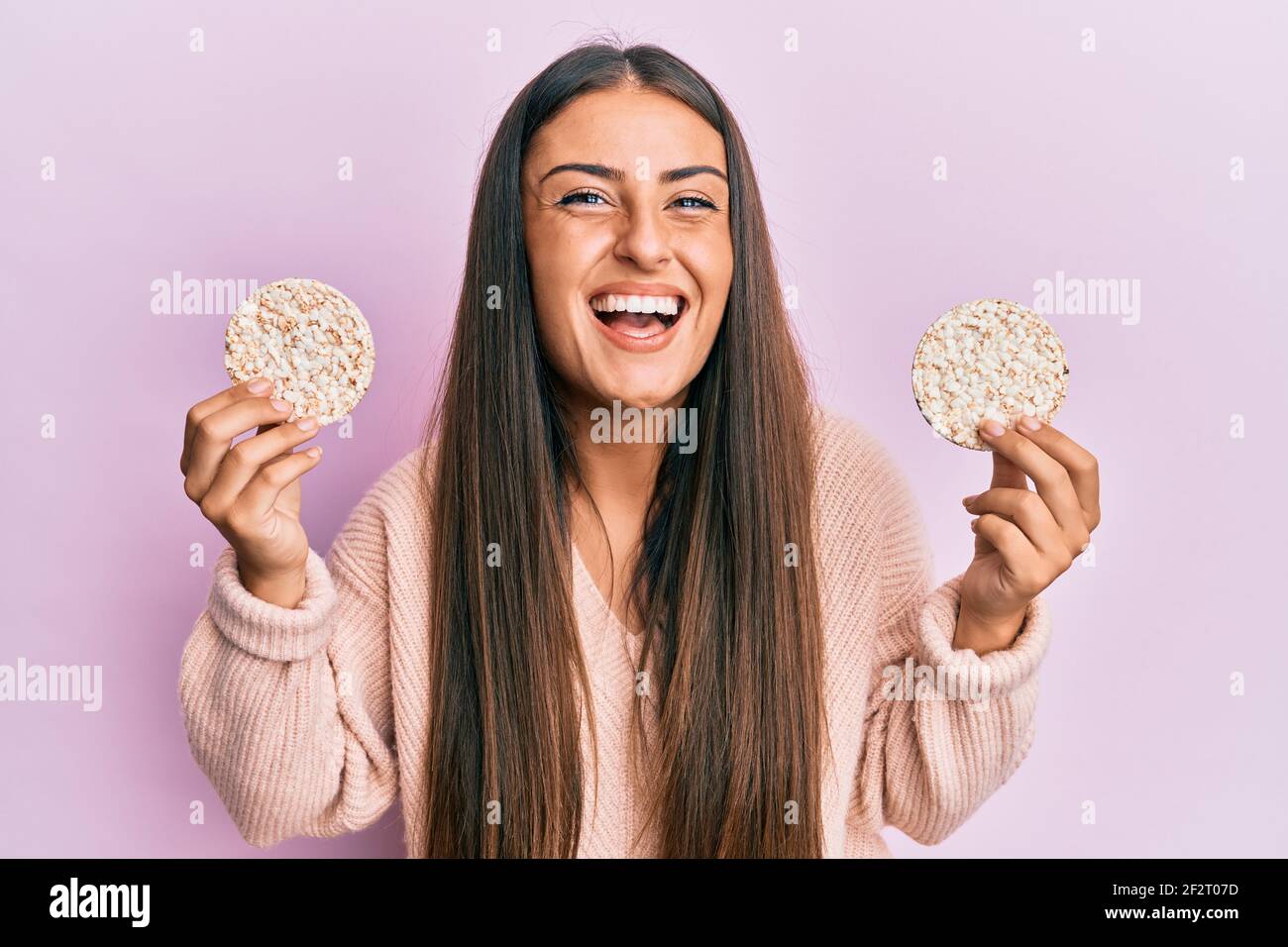 Beautiful hispanic woman eating healthy rice crackers smiling and ...