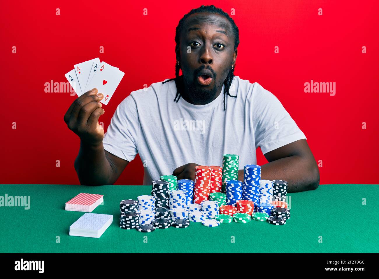 Handsome young black man playing poker holding cards scared and amazed ...