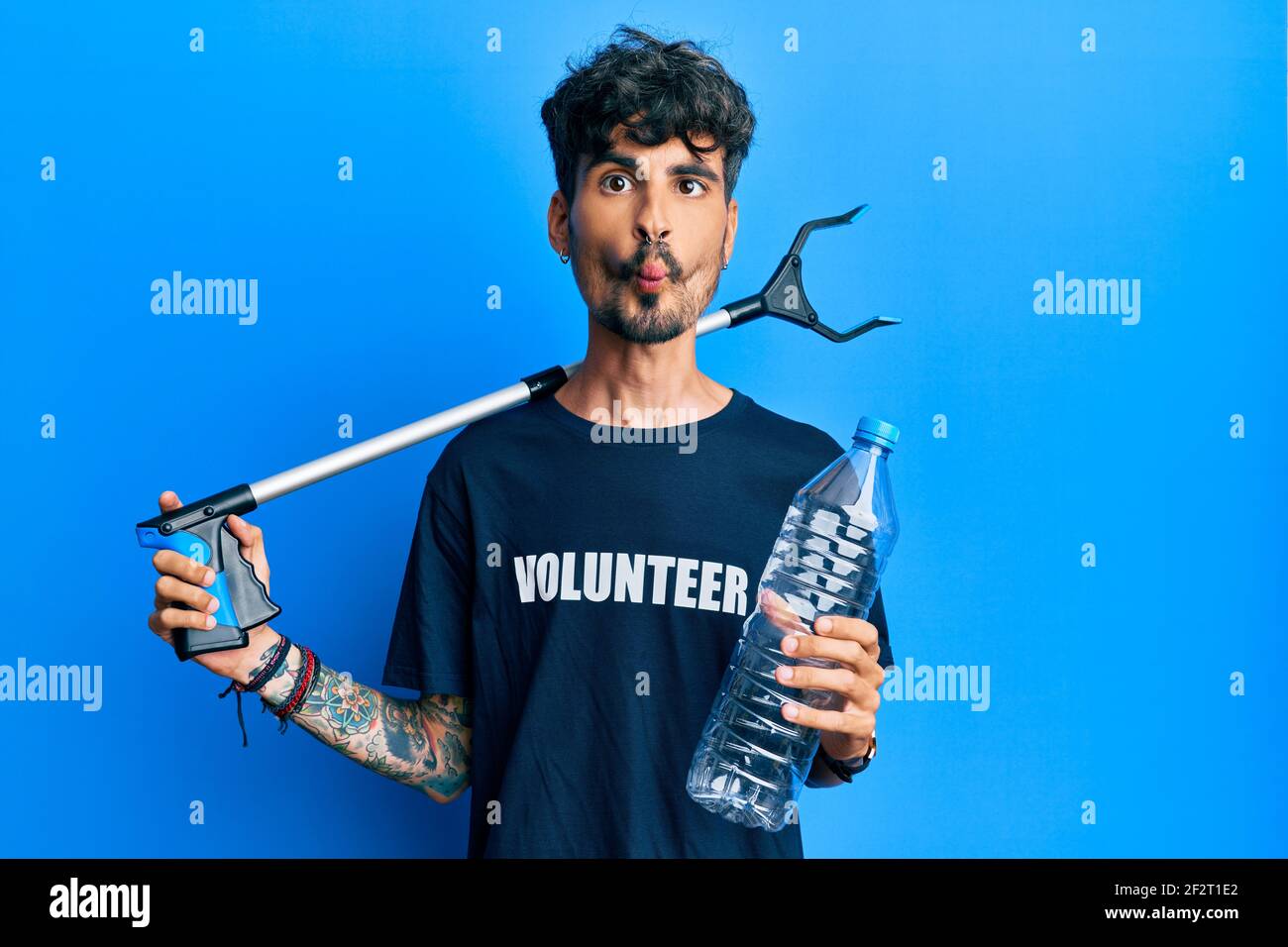 Young hispanic man holding plastic bottle and litter picker to recycle ...