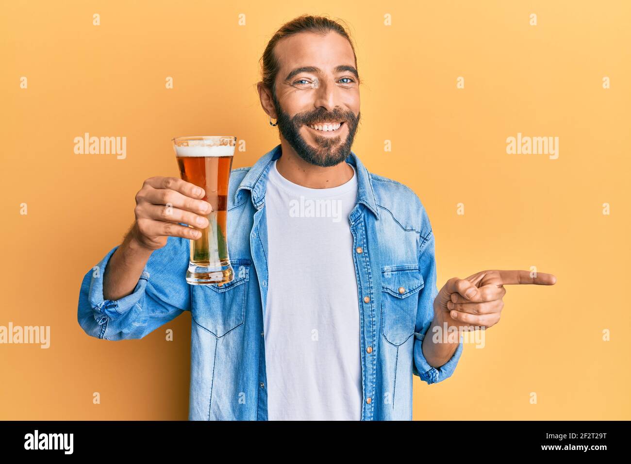 Attractive man with long hair and beard drinking a pint of beer smiling ...