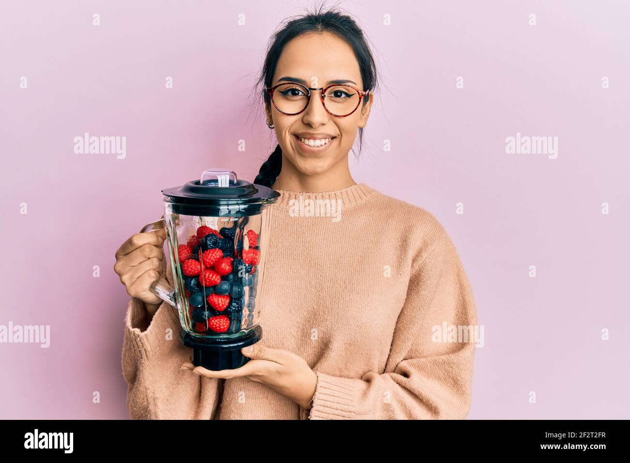 Young hispanic girl holding food processor mixer machine with fruits ...