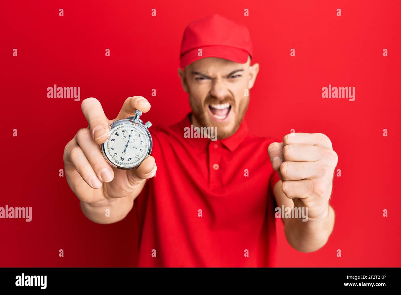 Young redhead man wearing delivery uniform and countdown clock annoyed ...