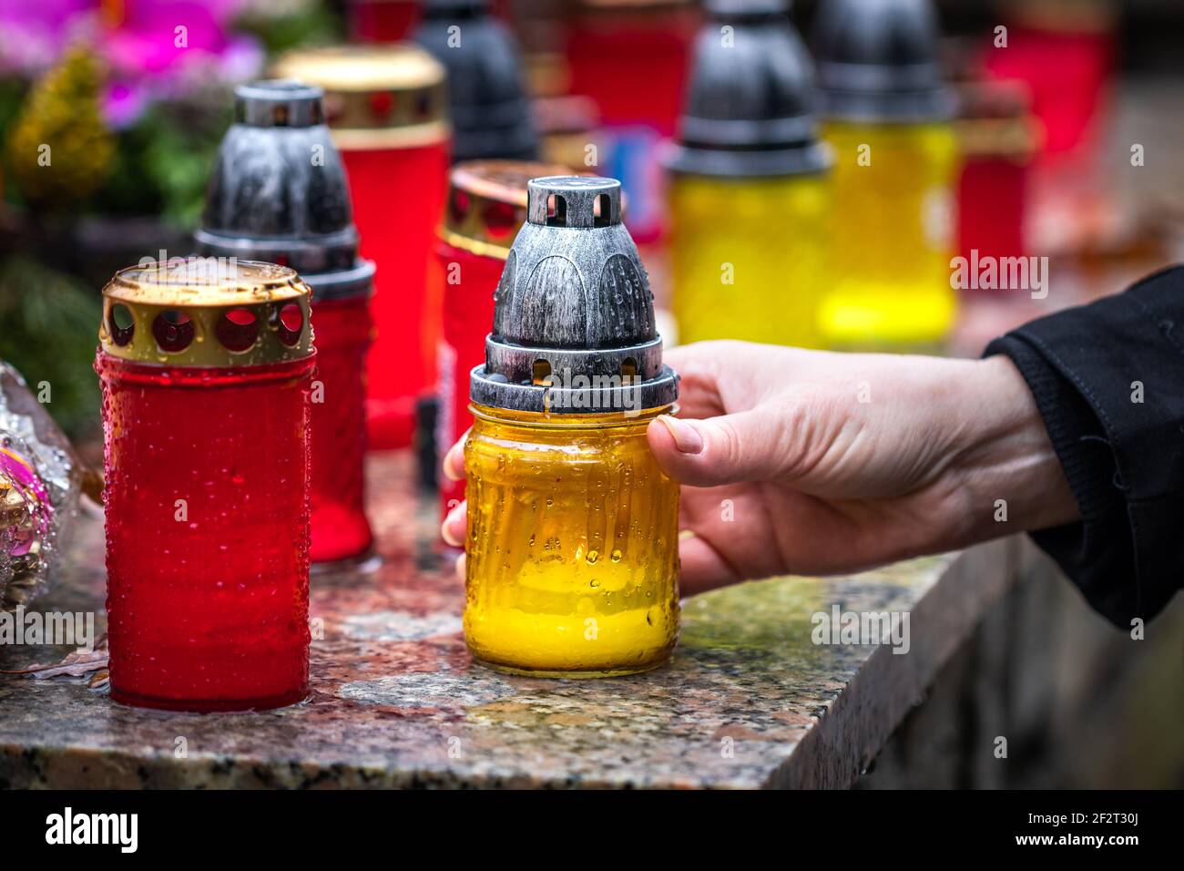 Woman is putting candle lantern at grave in cemetery. Grief for dead person. Close-up hand ...