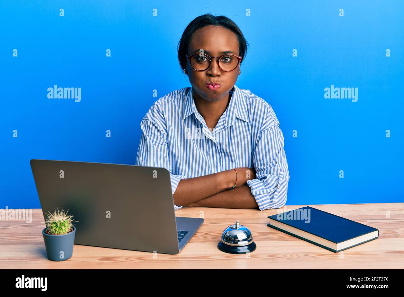 Young african woman working at hotel reception using laptop puffing ...