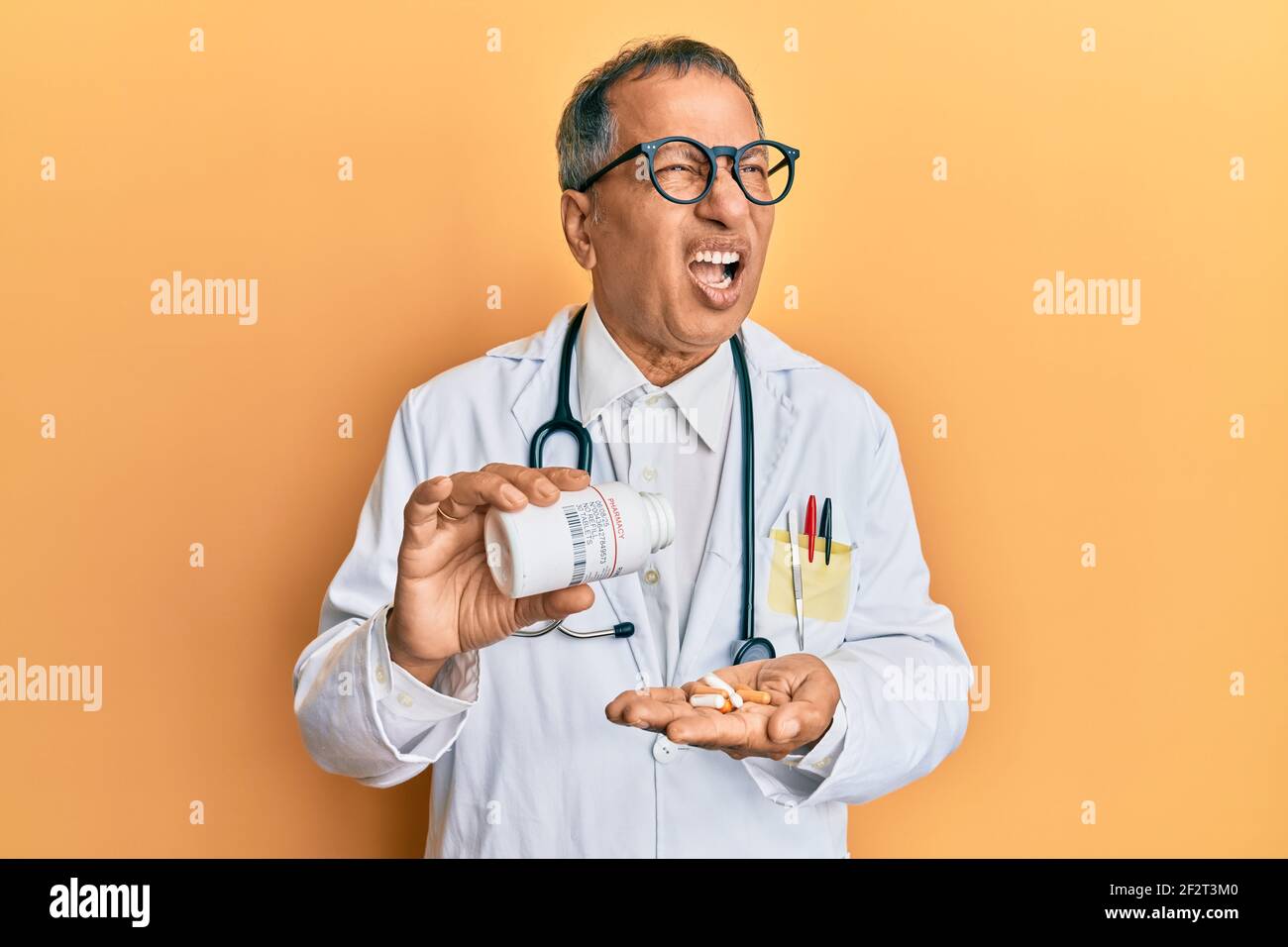 Middle age indian man wearing doctor uniform holding prescription pills ...
