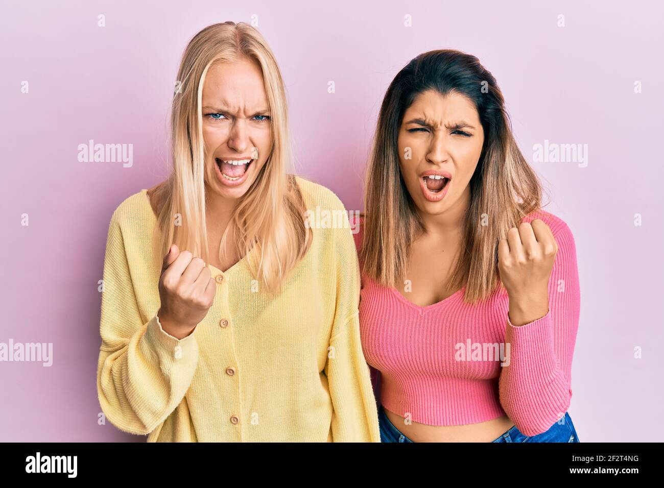 Two friends standing together over pink background angry and mad ...