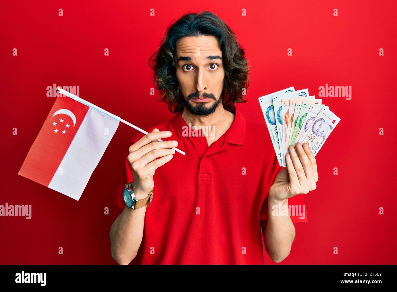 Young hispanic man holding singapore flag and dollars depressed and ...