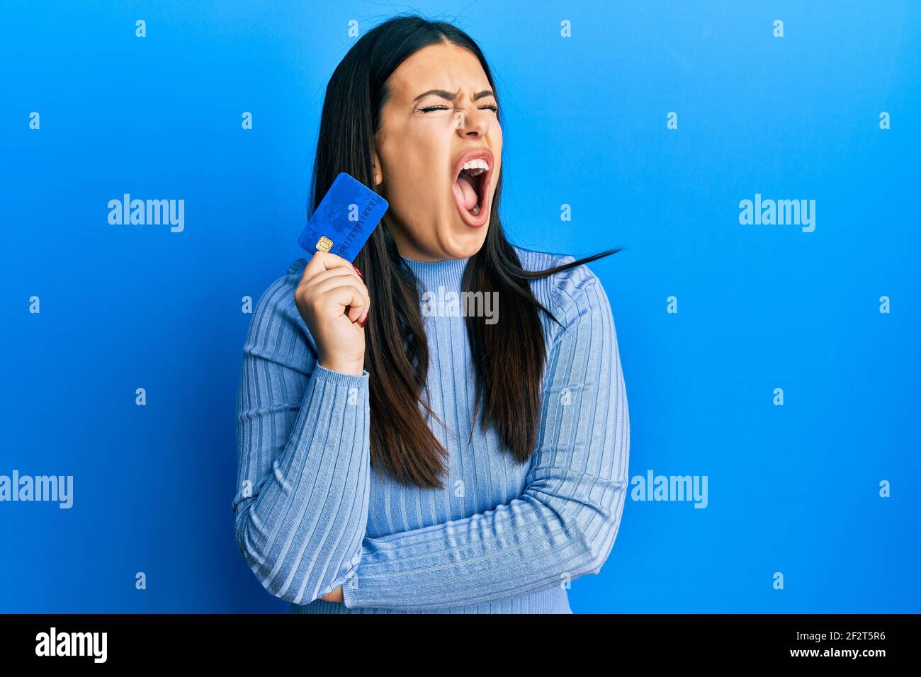 Beautiful brunette woman holding credit card angry and mad screaming ...