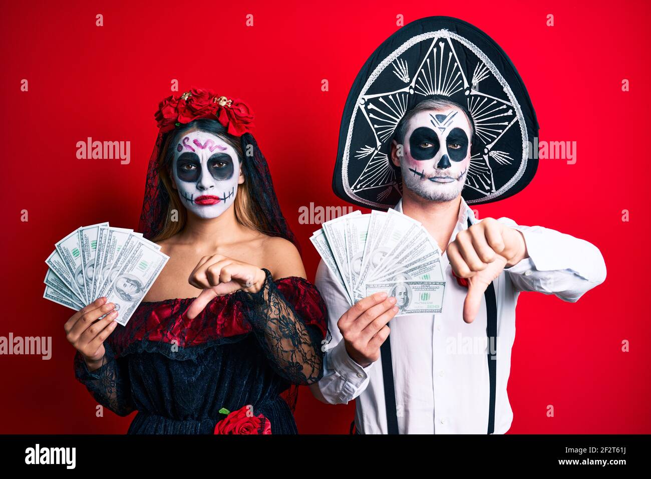 Couple wearing day of the dead costume holding dollars with angry face ...
