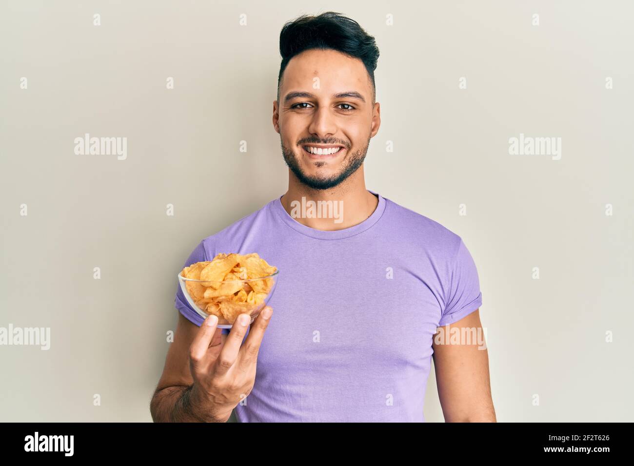 Young arab man holding potato chip looking positive and happy standing ...