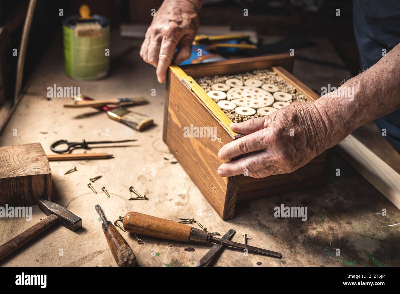 Craftsperson measuring insect hotel by folding meter. Old man working ...
