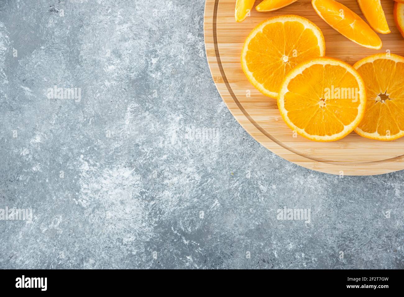 A wooden board full of juicy slices of orange fruit on stone background ...