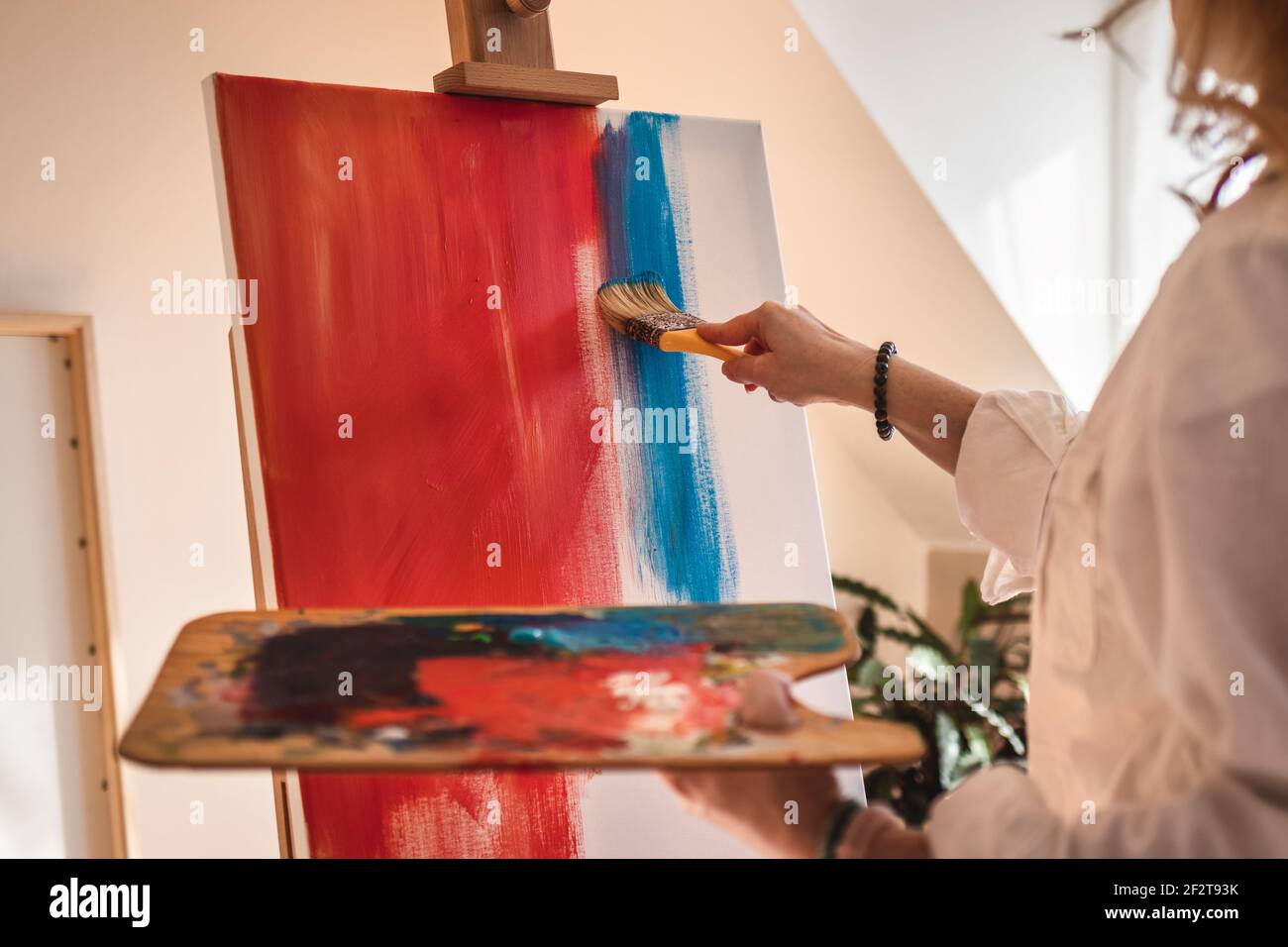 Woman painting in her art studio. Red and blue acrylic paint on canvas ...