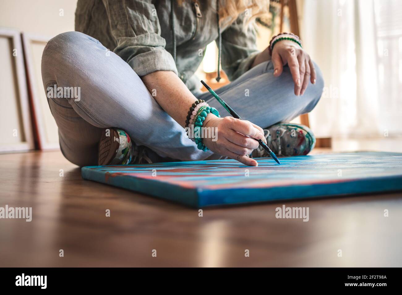 Artist painting in her art studio. Woman sitting on floor and working ...