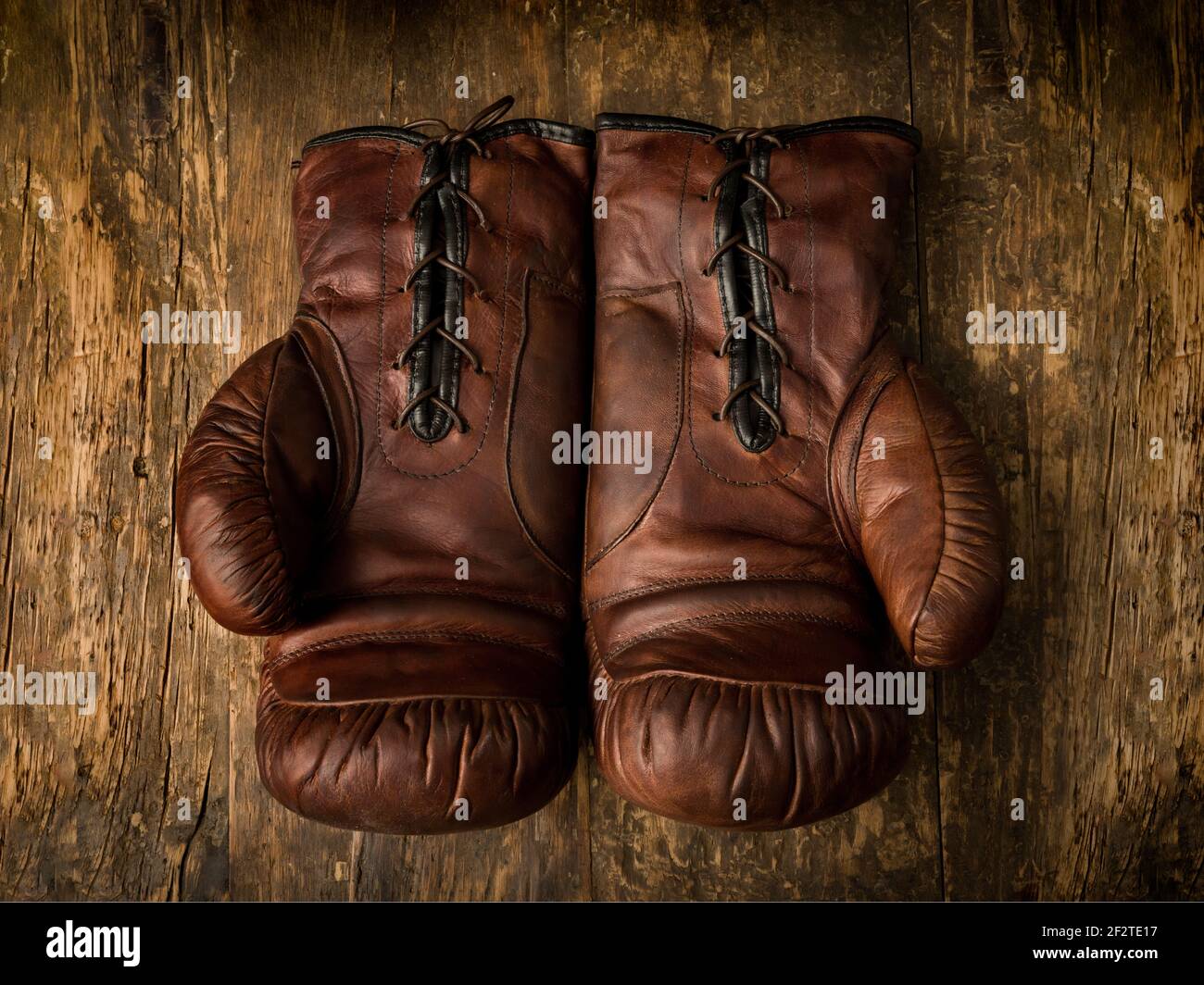Pair of old brown leather boxing gloves lying on an antique wooden ...