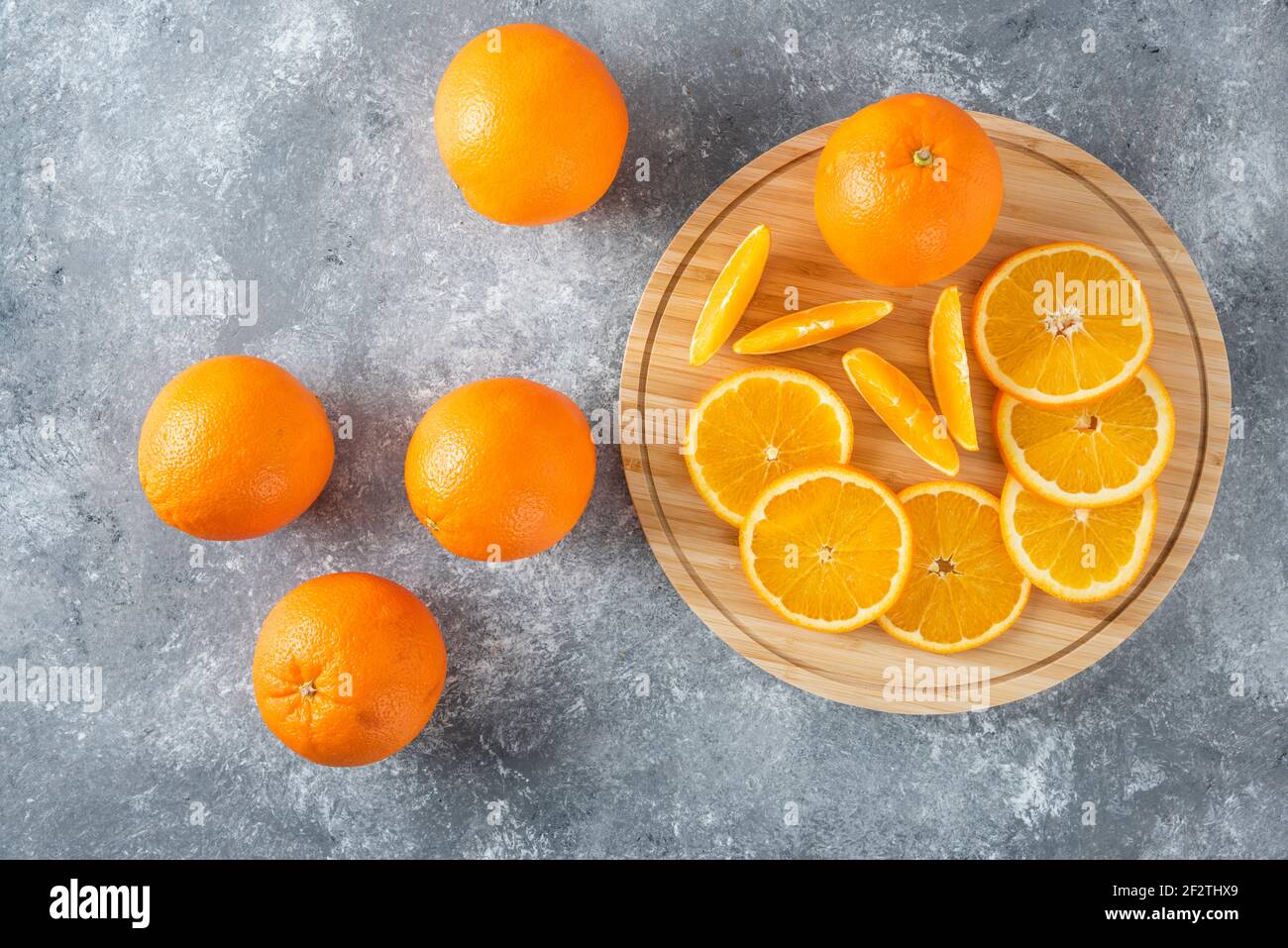 A wooden board full of juicy slices of orange fruit on stone background ...