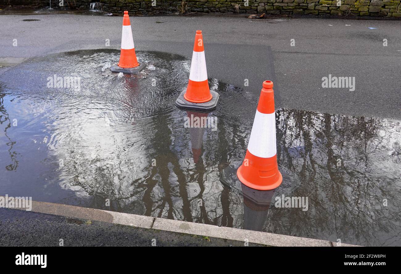 Bollards on a road in New Mills show water spurting through the road ...