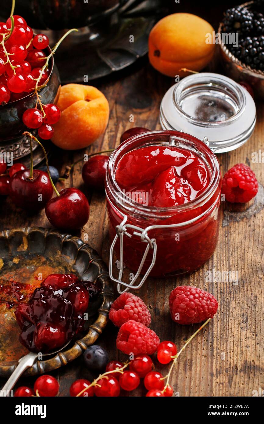 Jar of strawberry jam among summer and autumn fruits on a wooden table ...