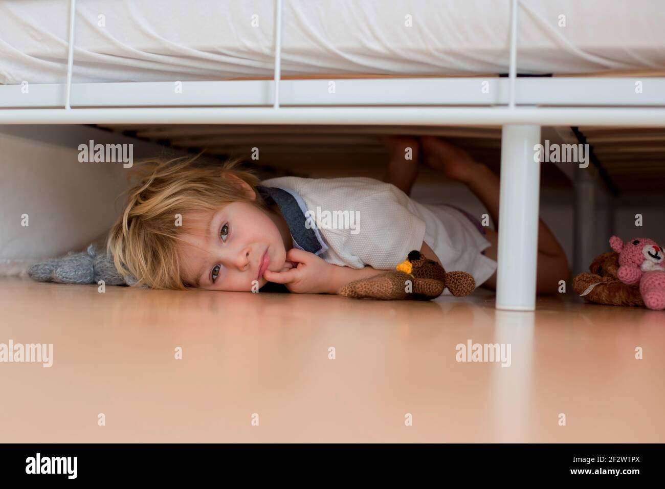 Little toddler child, hiding under the bed with stuffed toys, scared ...