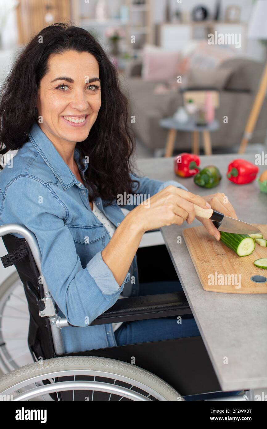 disabled woman preparing vegetables while sitting in wheelchair near ...