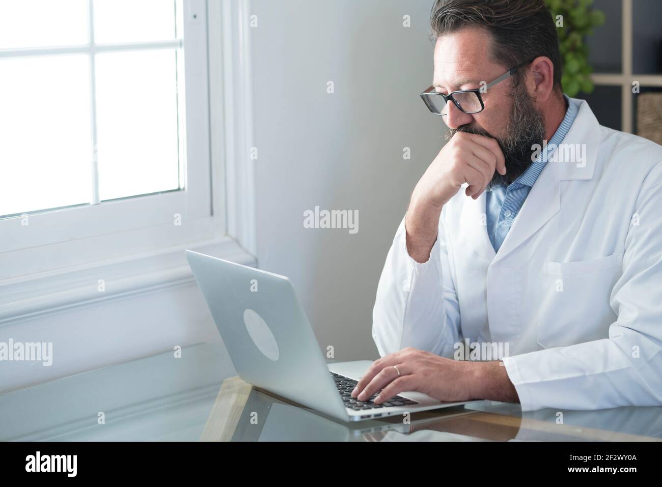 Mature doctor sitting in office. Adult doc in white coat write and work ...