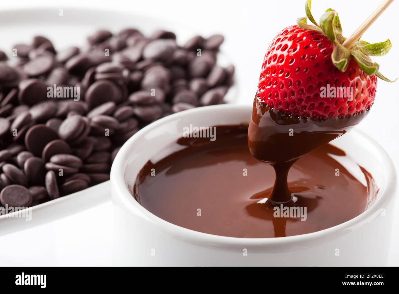 Strawberry being dipped in dark chocolate isolated in studio with white ...