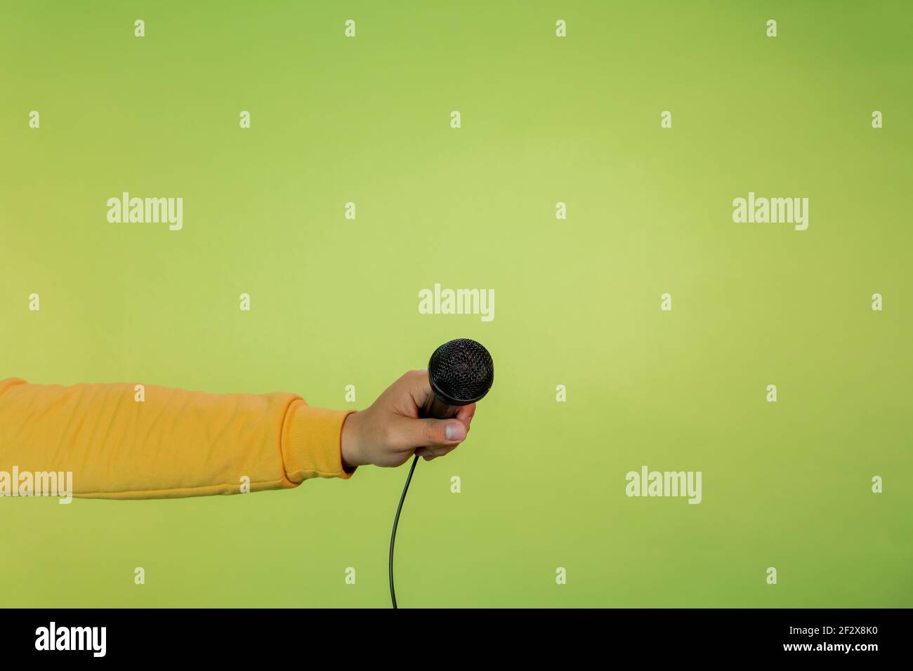 An isolated hand holding a microphone on an empty green background for ...