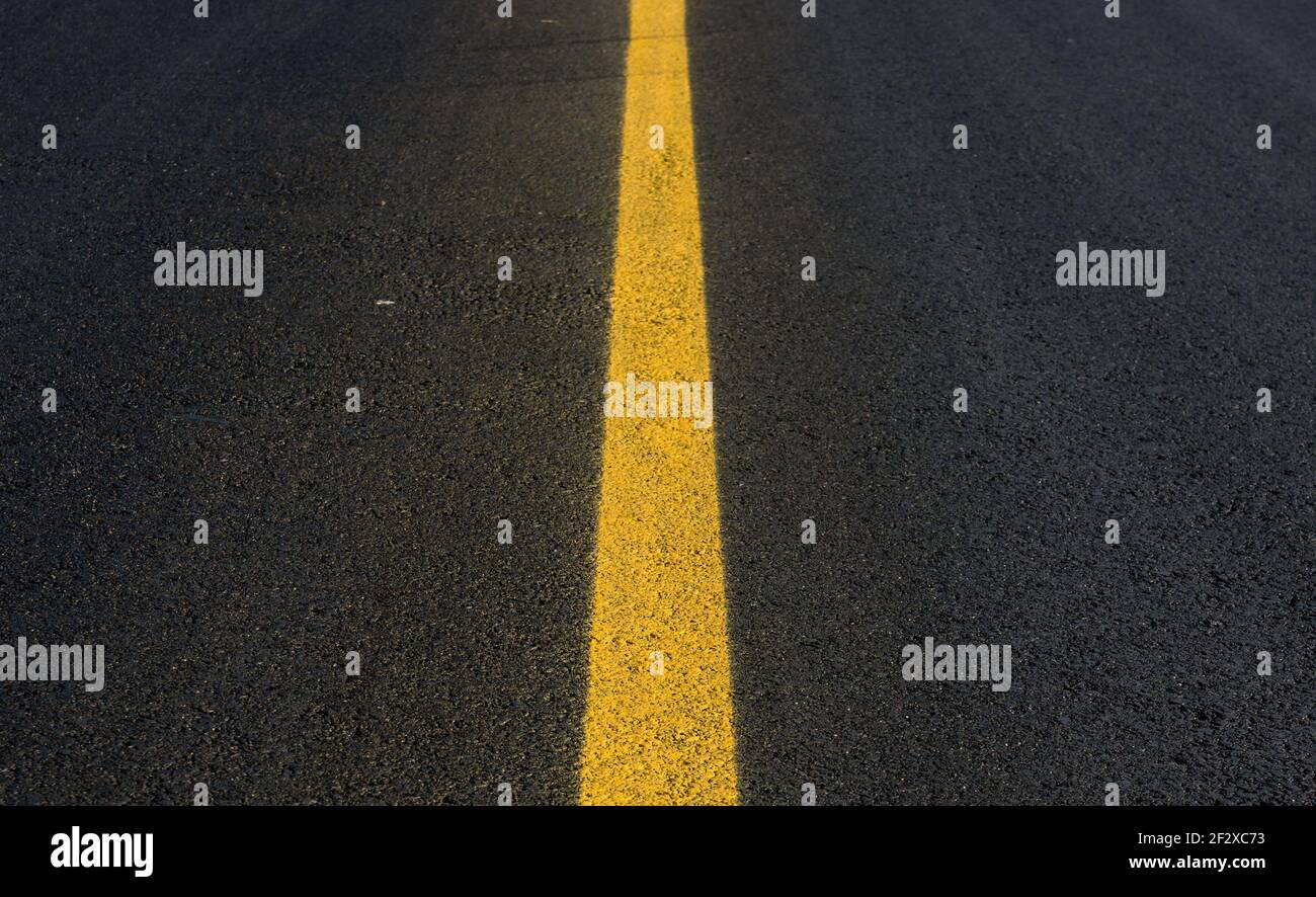 A yellow line in the middle of a black asphalt road. Only the line and ...