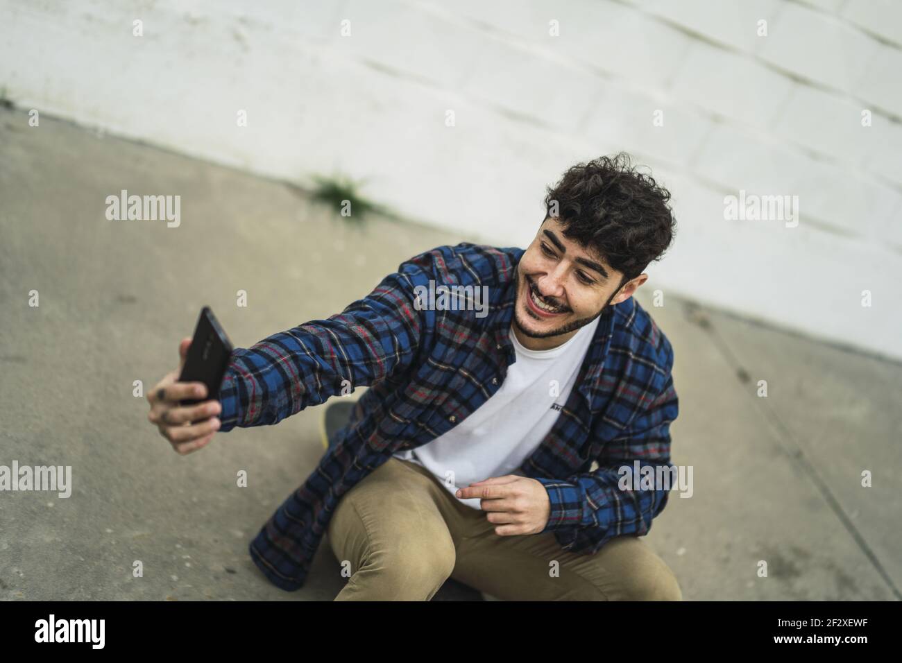 An attractive Spanish male taking a selfie sitting on an asphalt Stock ...