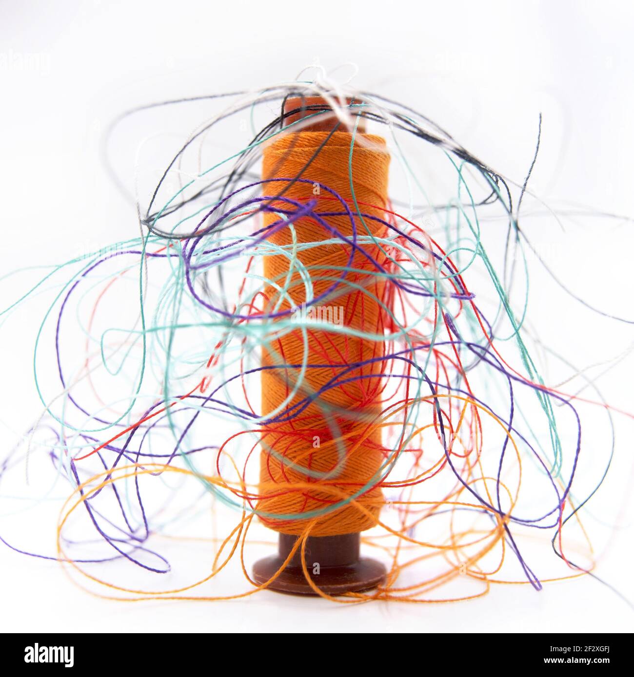 A spool of orange thread and colorful string on a white background ...