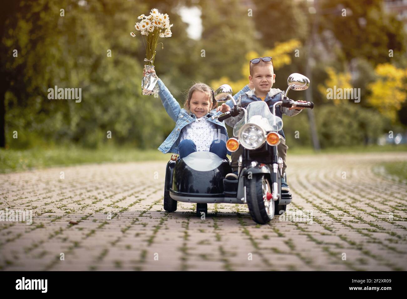 cute caucasian boy driving little girl in sidecar of motorcycle toy on ...
