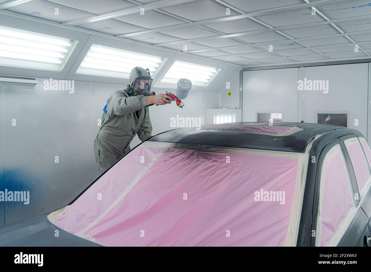 Side view of male in respiratory mask and protective suit painting car ...