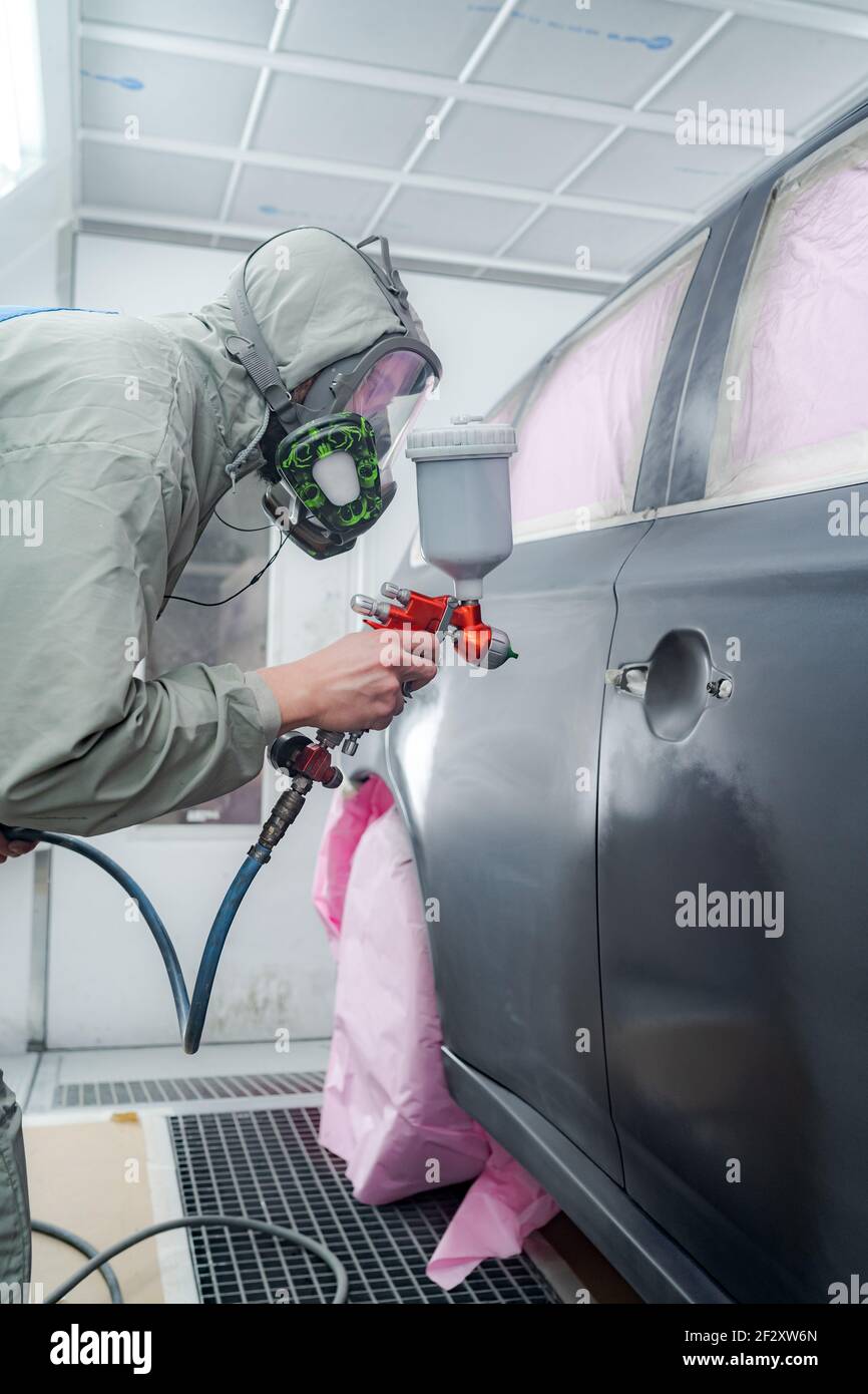 Side view of male in respiratory mask and protective suit painting car ...