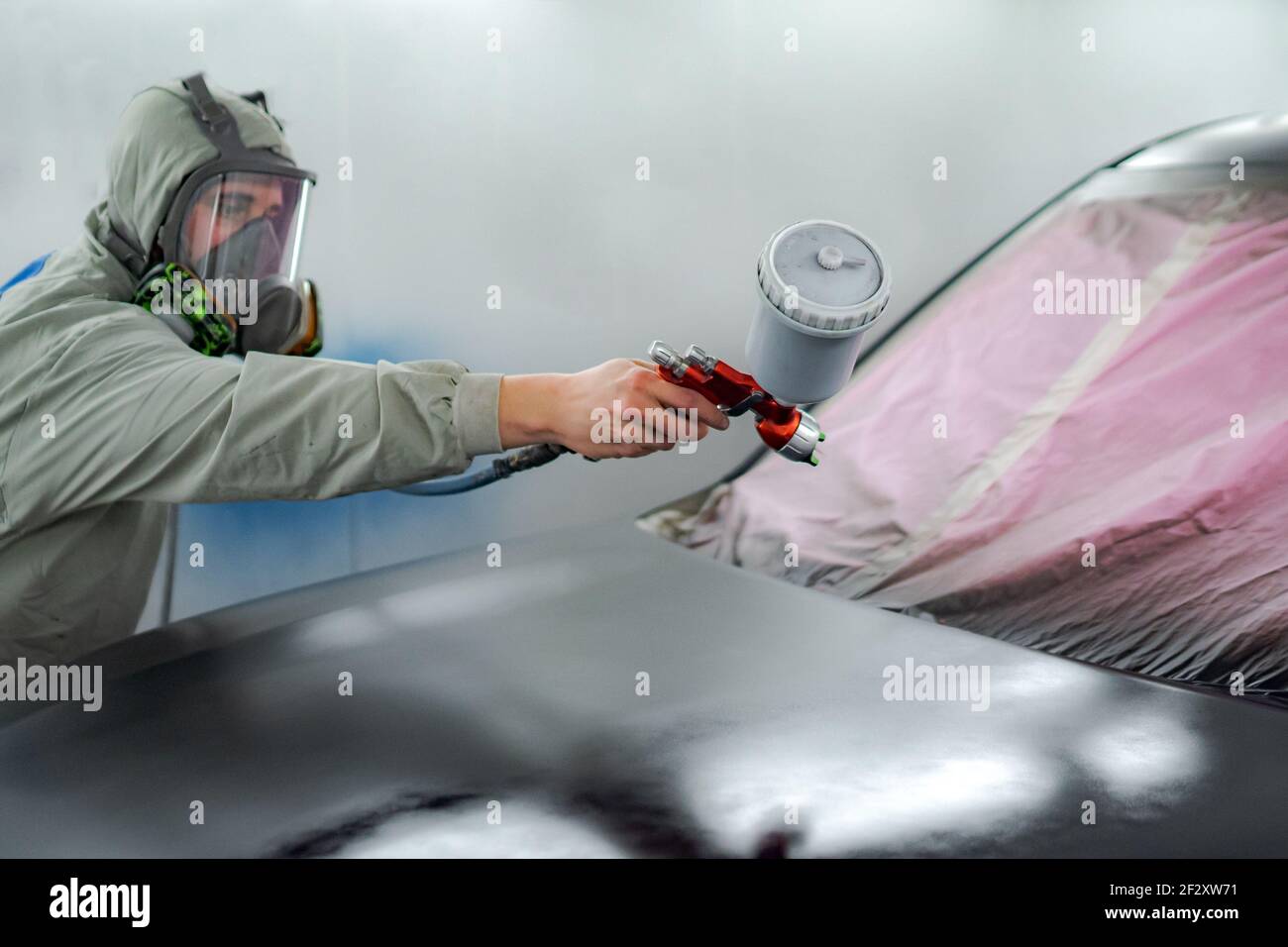 Side view of male in respiratory mask and protective suit painting car ...