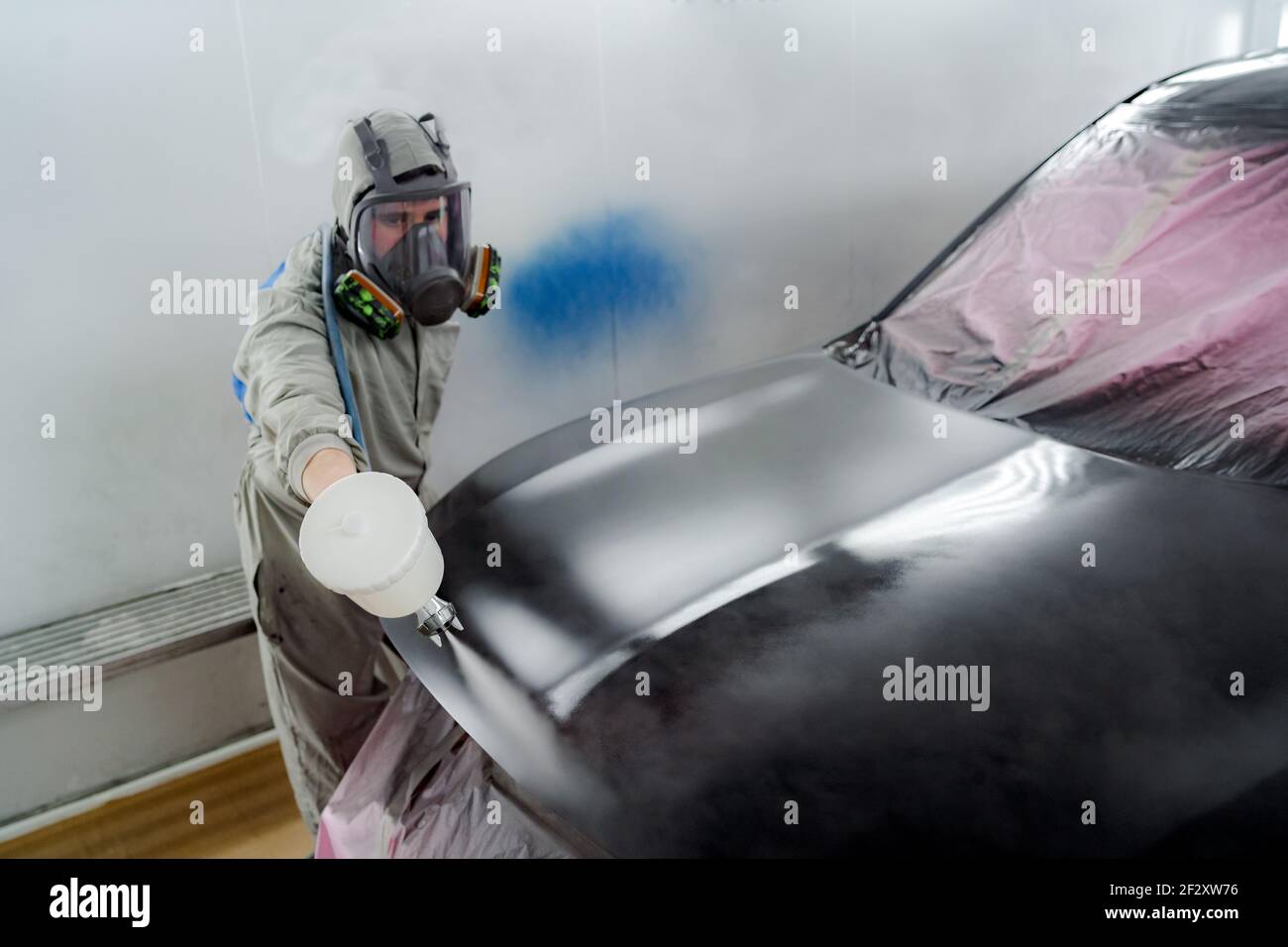 From above male in respiratory mask and protective suit painting car ...