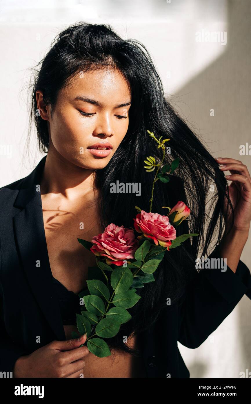 Young charming ethnic female model wearing black robe touching hair ...