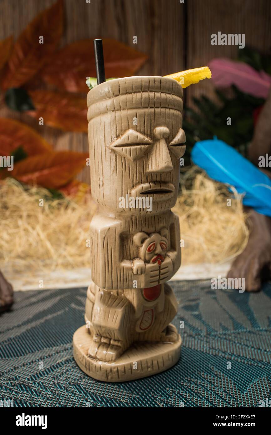 Traditional sculptural tiki cup of alcohol drink with straw placed on ...