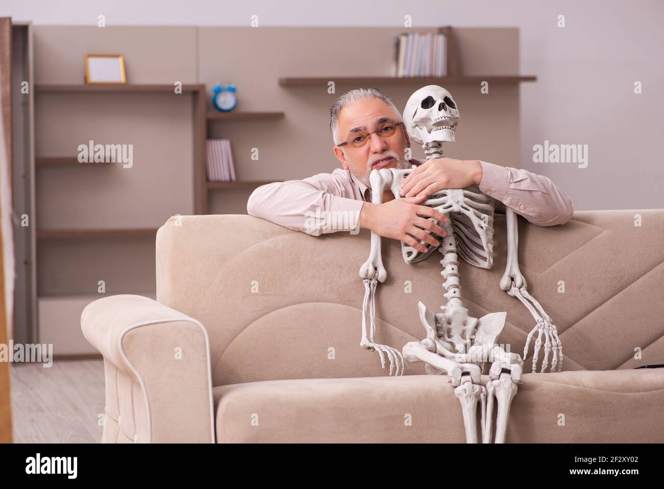 Old man sitting on the sofa with the female skeleton in undying love ...