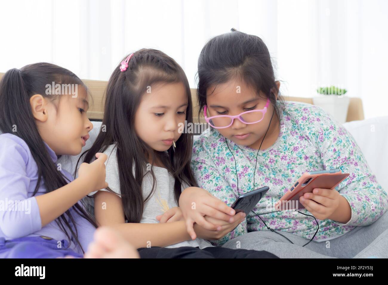 Happy asian little kid and friends playing smartphone on sofa at home ...