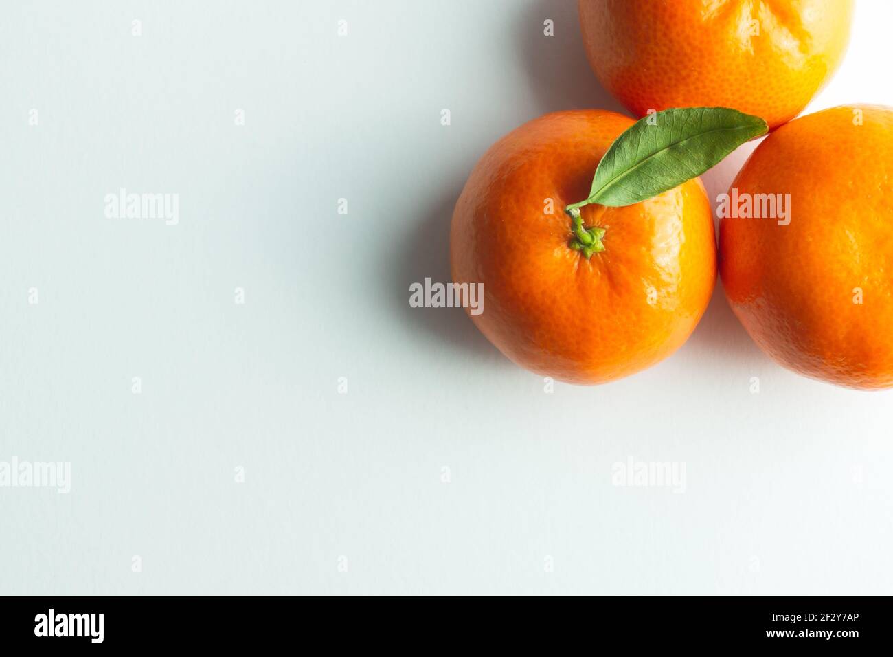 three tangerines with green leaf in the upper right on white background ...