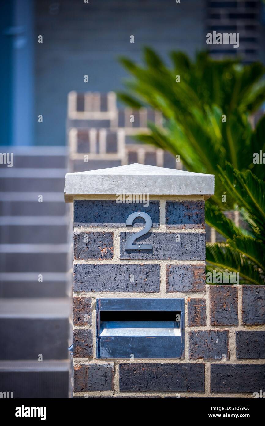 Metallic number 2 on grey brick garden walls contrast with green palms ...