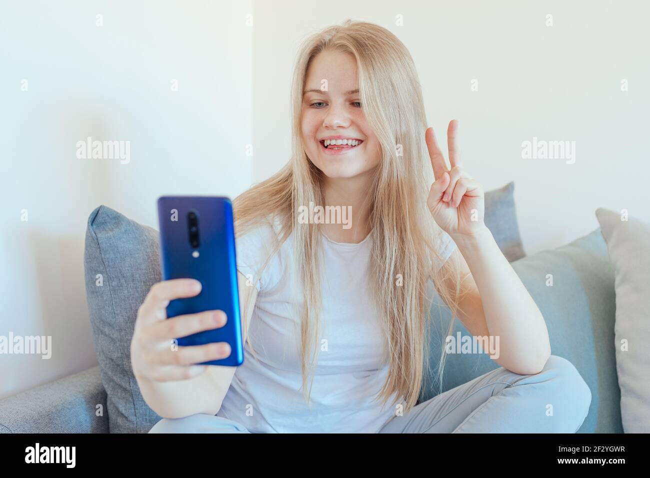 Young, smiling girl taking a positive selfie and showing a peace sign ...