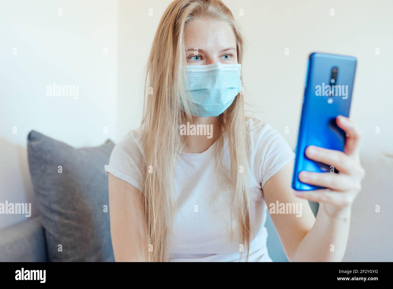 Blonde girl on a self-isolation having a video call with smartphone ...