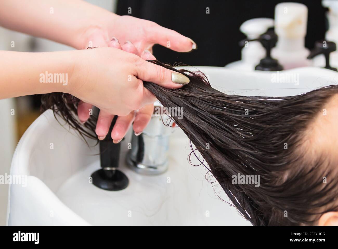 The hairdresser washes the head of a girl with long hair in the sink ...