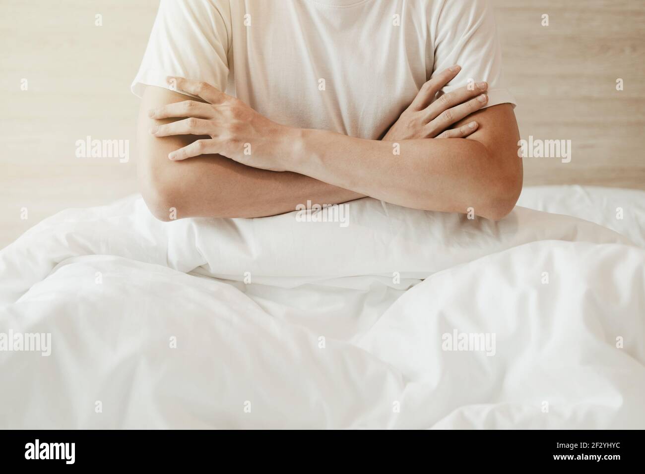 A man sitting on the bed and crossed arms on white bed in bedroom with ...