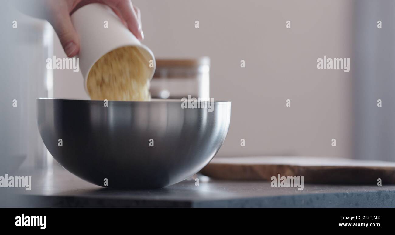 man making granola pour wheat flakes into steel bowl on kitchen ...