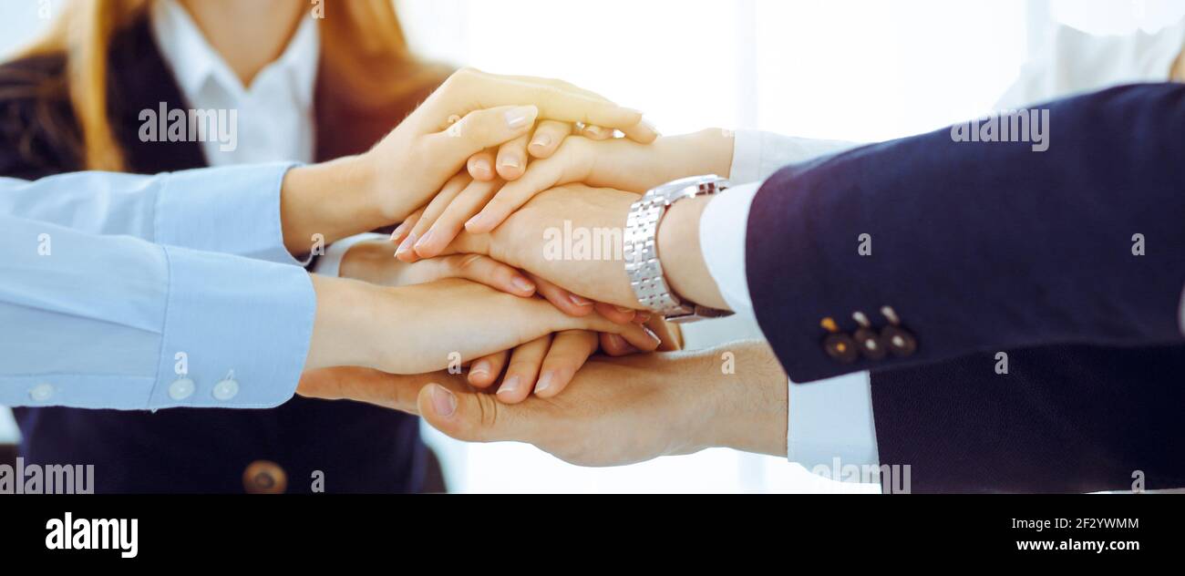 Business team showing unity with their hands together in sunny office. Group of people joining ...