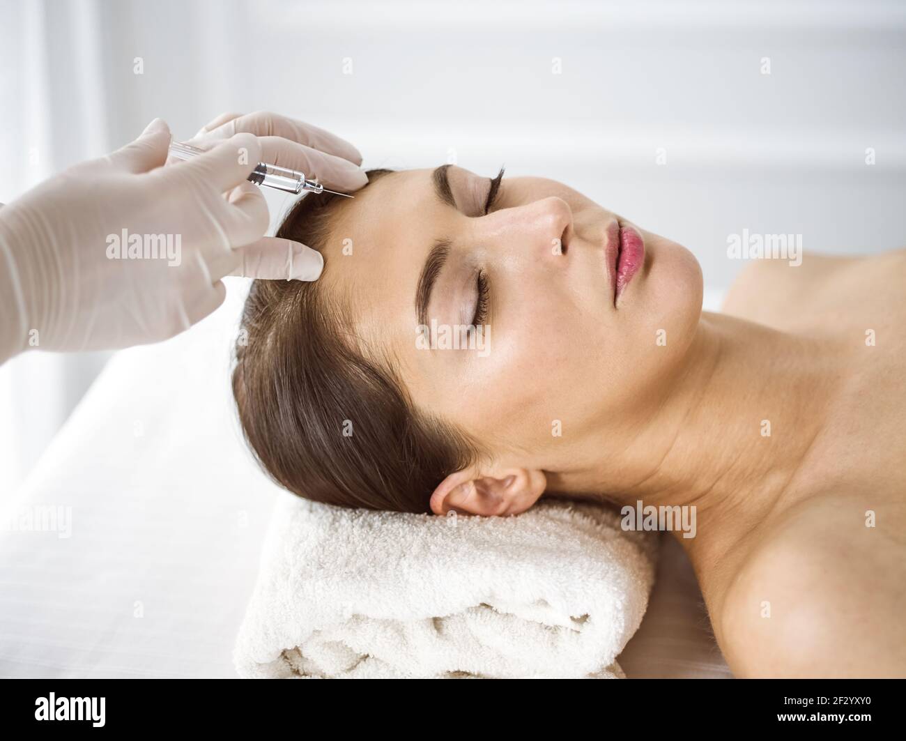 Beautician doing beauty procedure with syringe to face of young brunette woman in sunny clinic ...